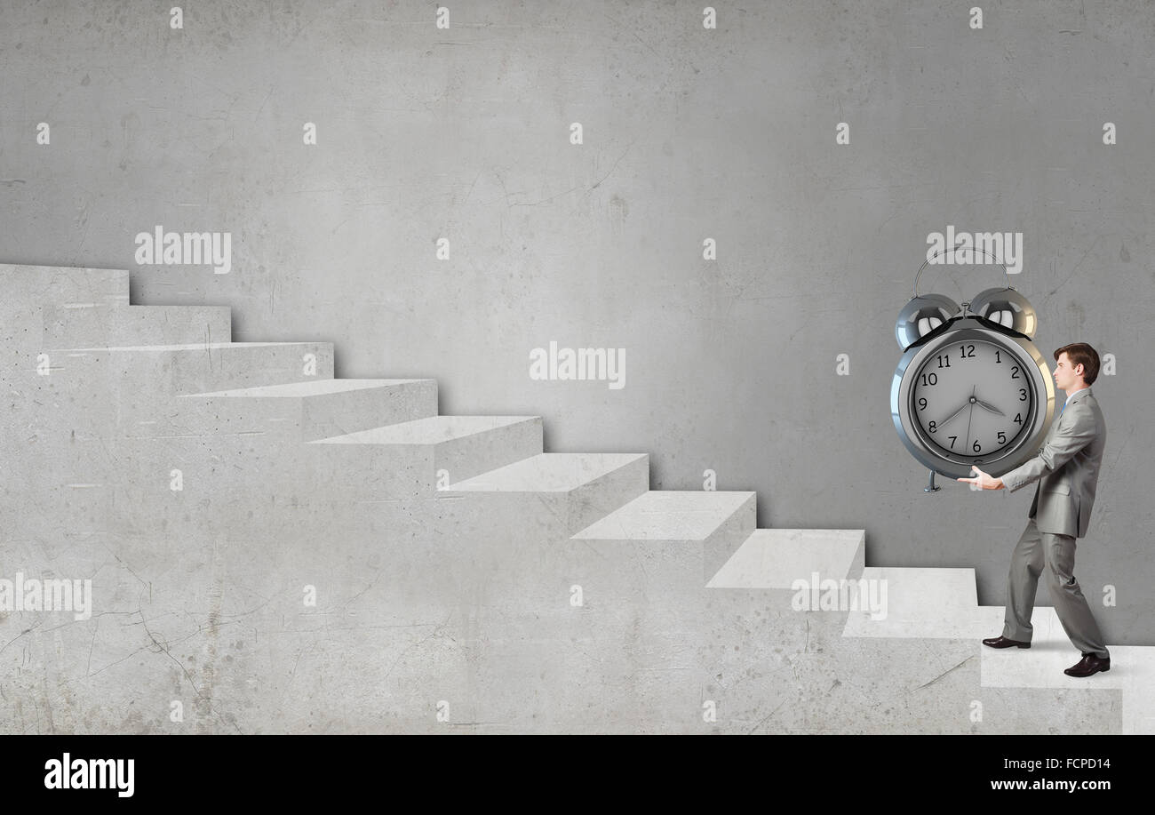 Young businessman carrying with effort huge alarm clock Stock Photo - Alamy