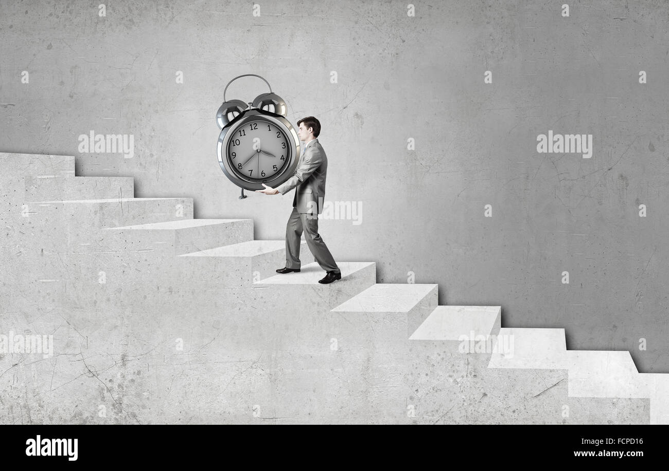 Young businessman carrying with effort huge alarm clock Stock Photo - Alamy