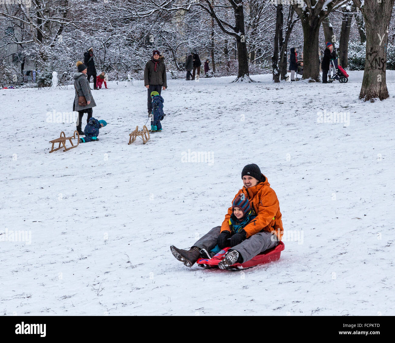 Father and child sledding on a snowy slope in a public park in winter ...