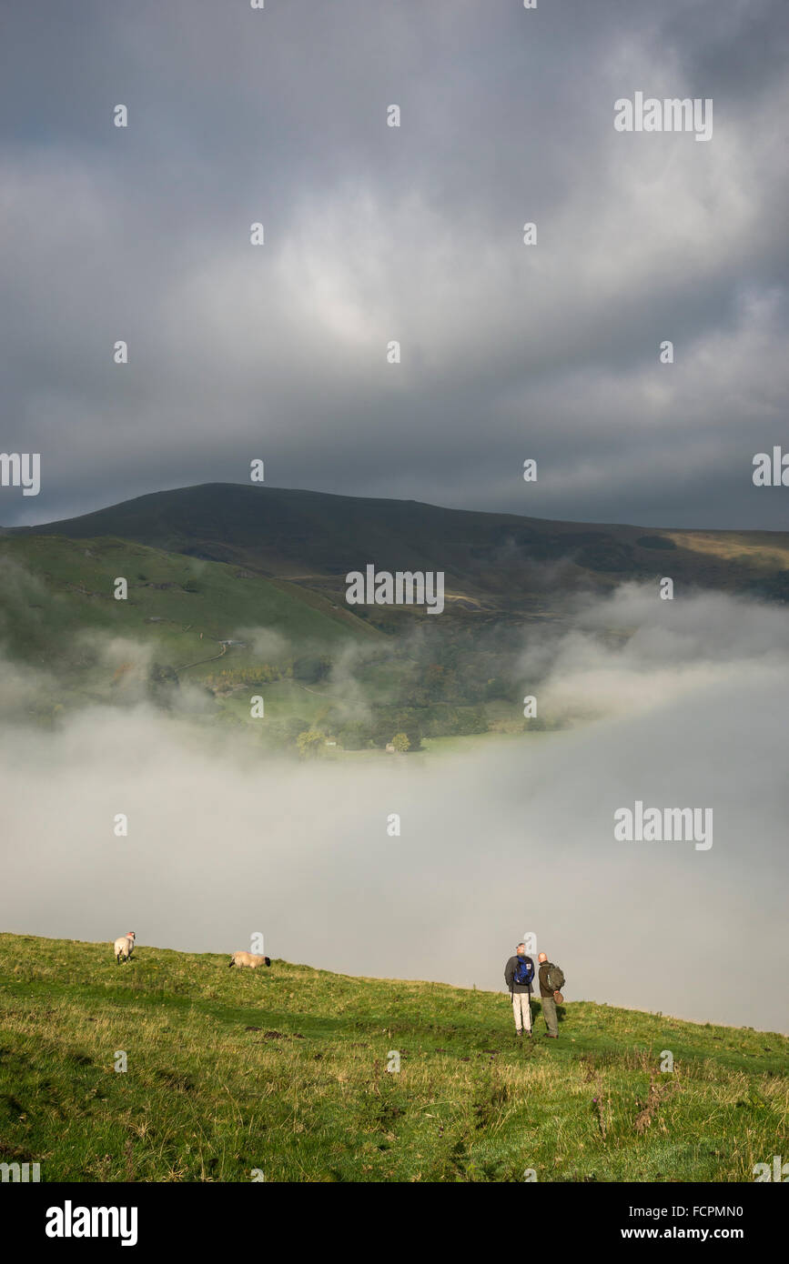 Two walkers stand and admire the view of mist below Mam Tor in ...