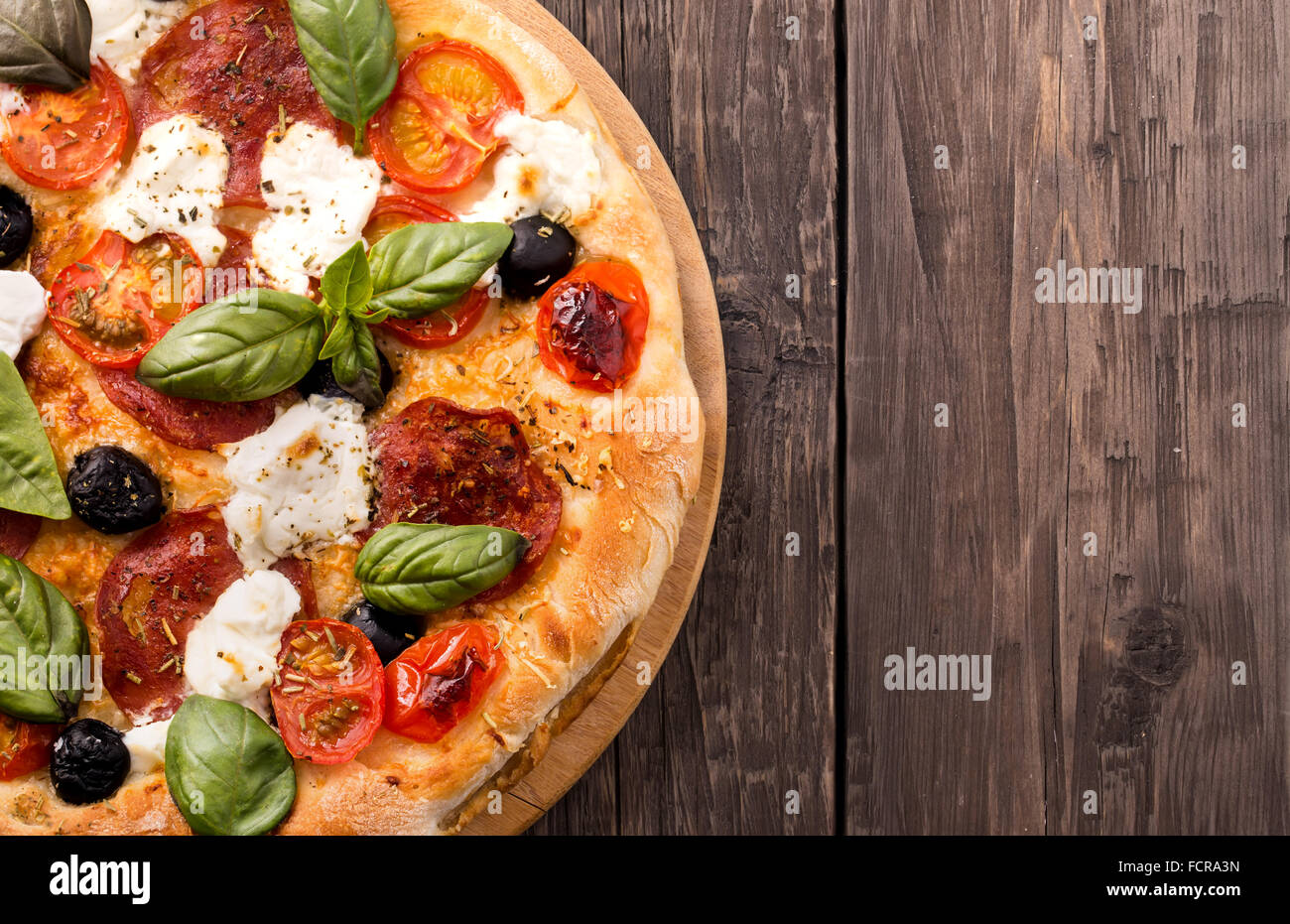 Rustic pizza with salami, mozzarella, olives and basil top view with ...