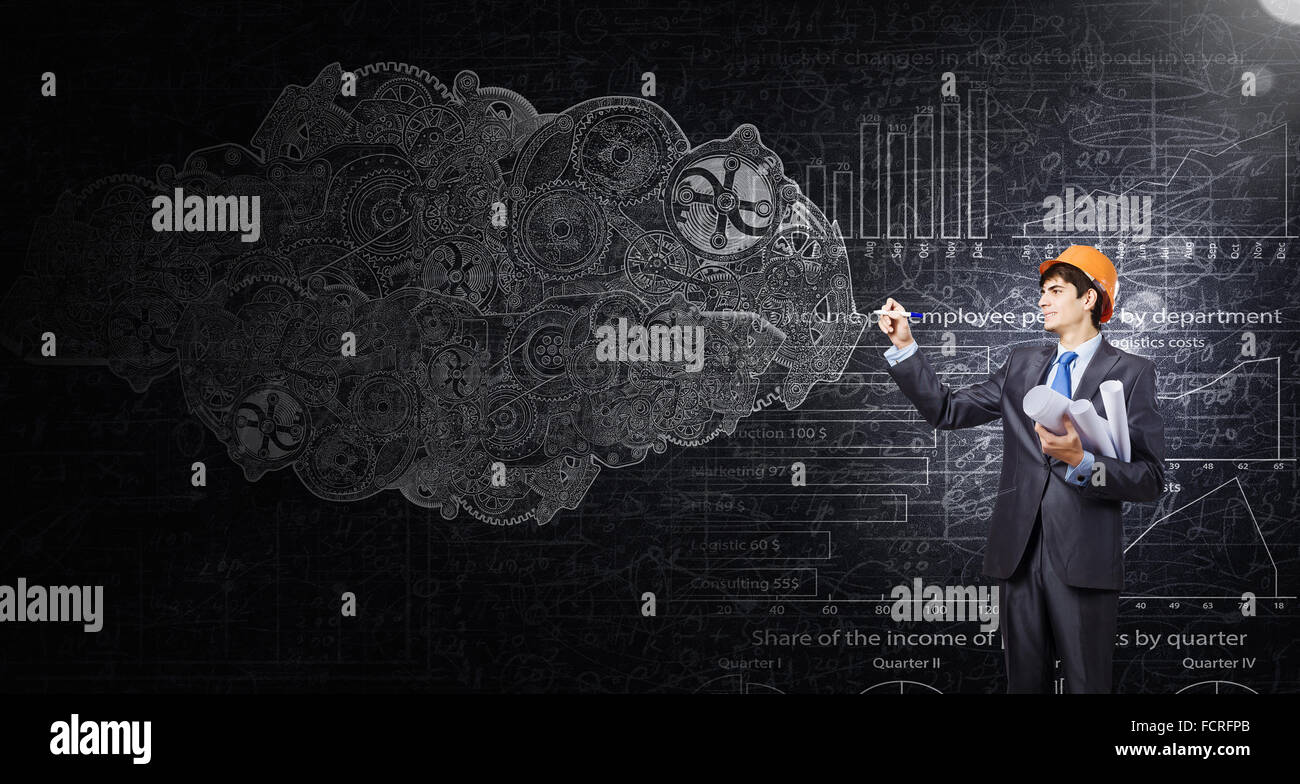 Engineer in helmet drawing gears on black wall Stock Photo - Alamy