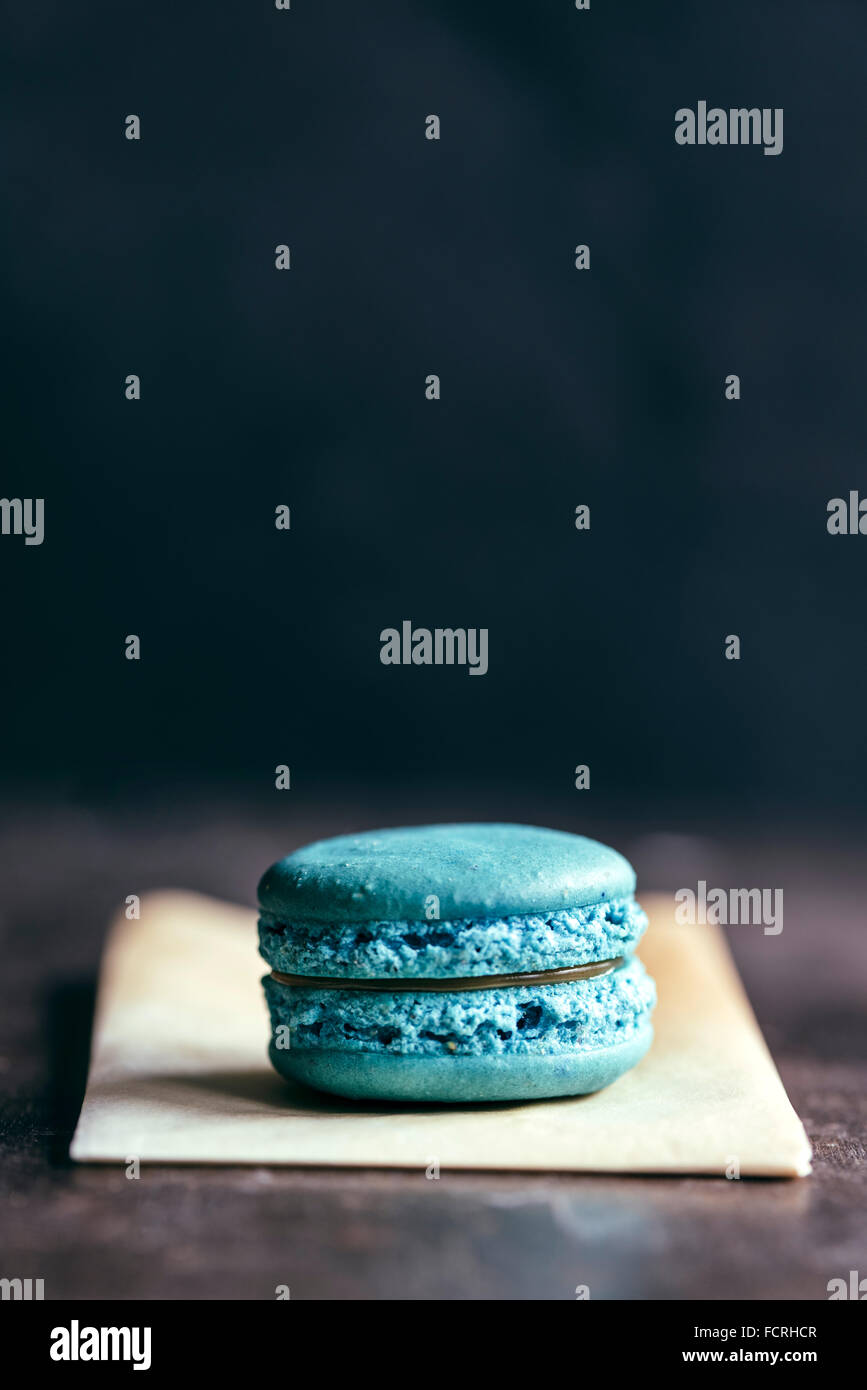 Single blue macaroon cookie on dark background with blank spae ...