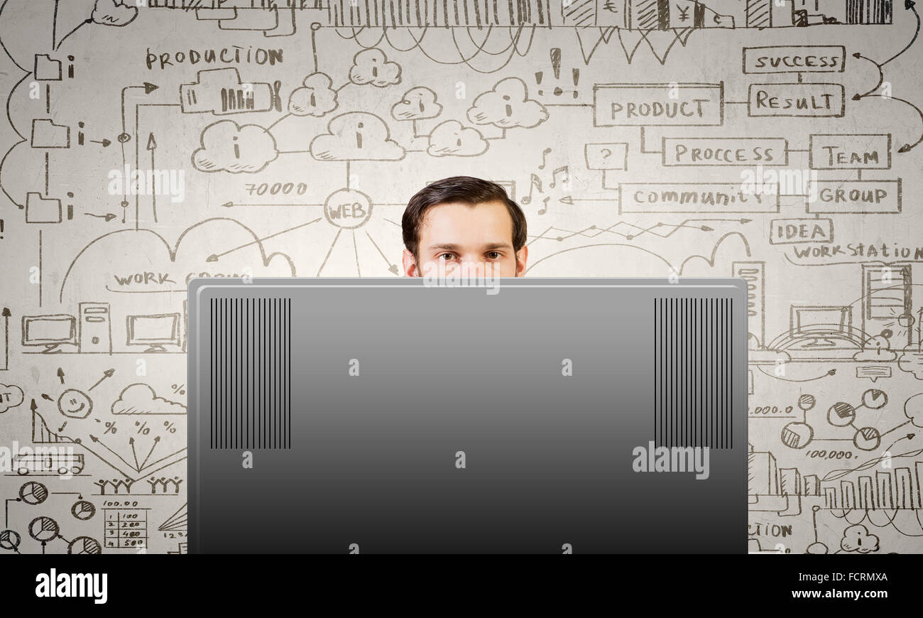 Young man looking out above laptop monitor Stock Photo - Alamy