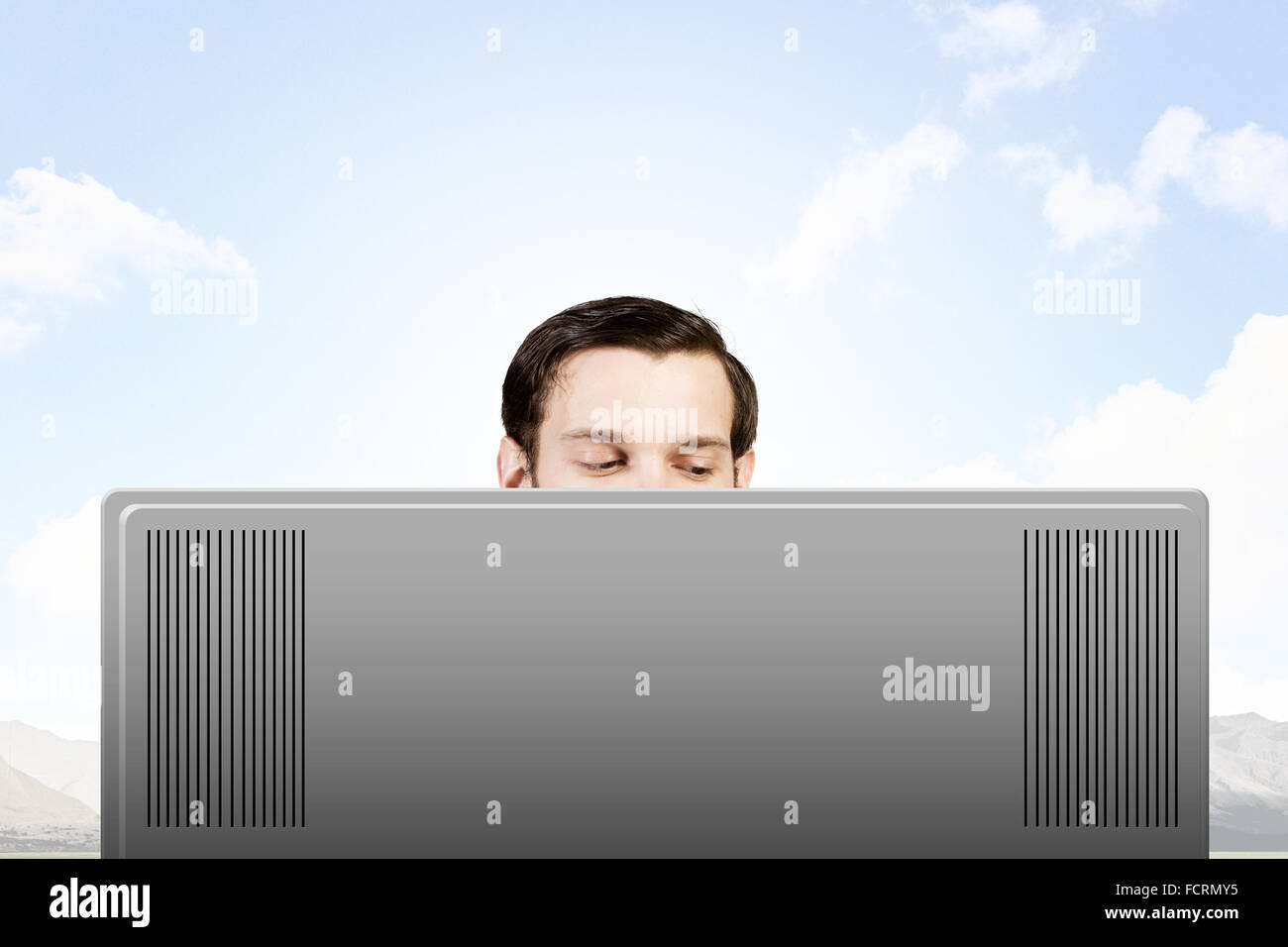 Young man looking out above laptop monitor Stock Photo - Alamy