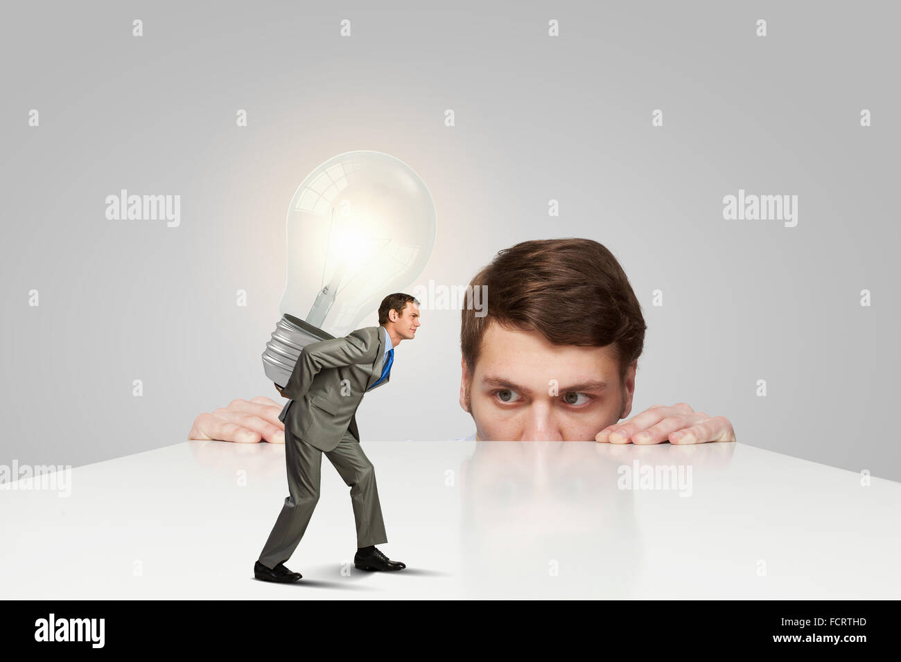 Young man looking from under table on man carrying bulb Stock Photo - Alamy