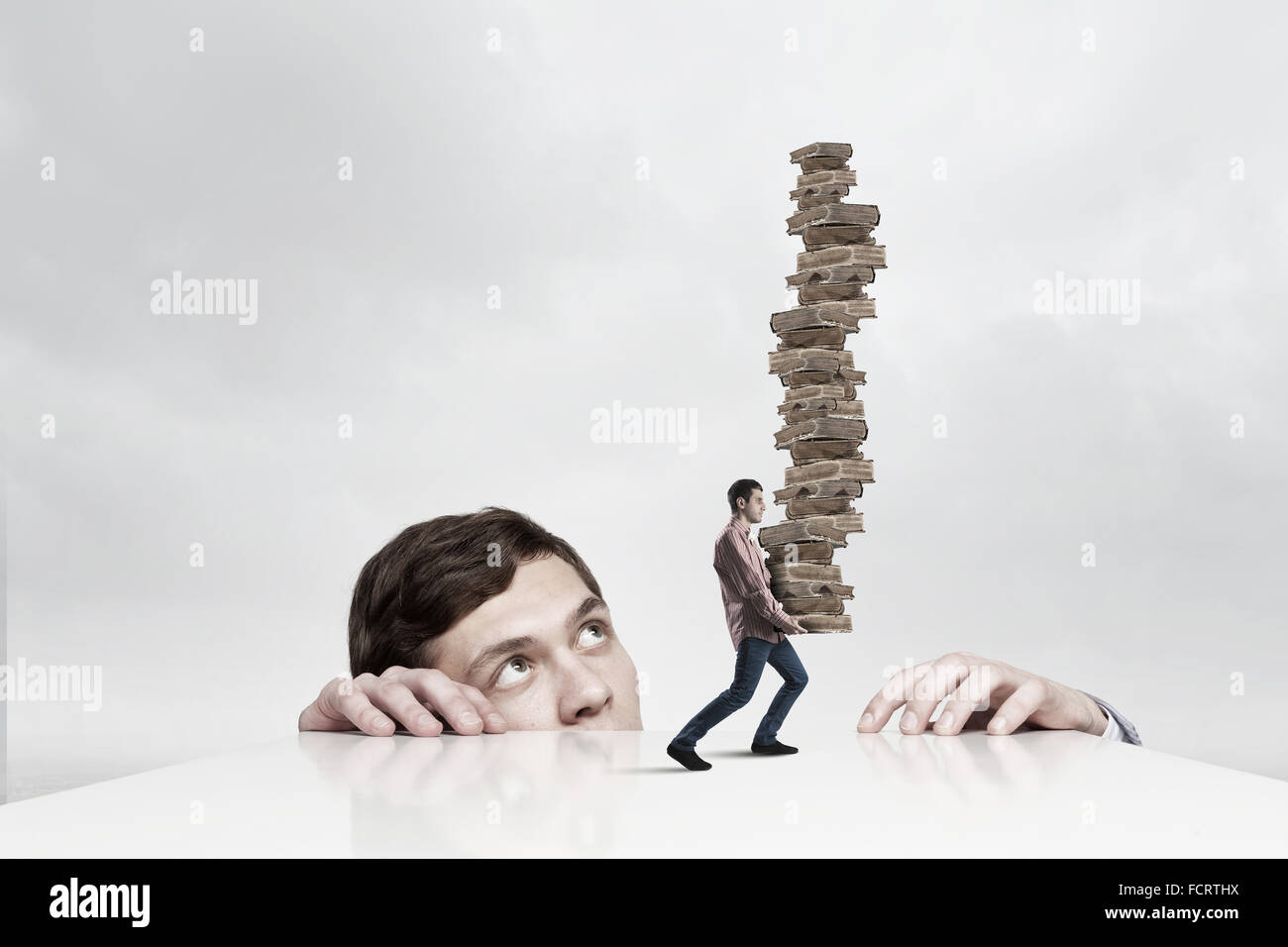 Young man looking from under table on student carrying pile of books ...