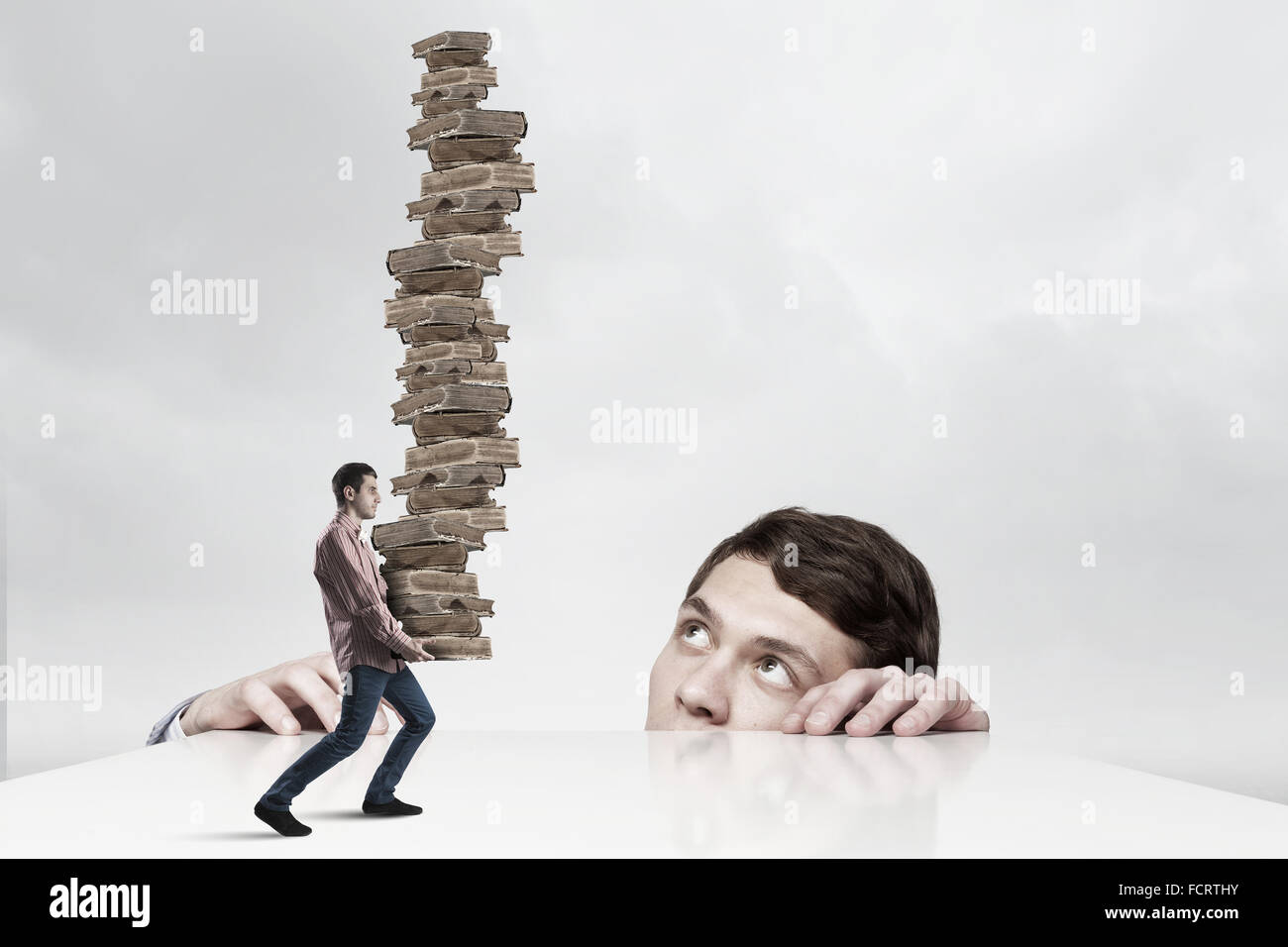 Young man looking from under table on student carrying pile of books ...