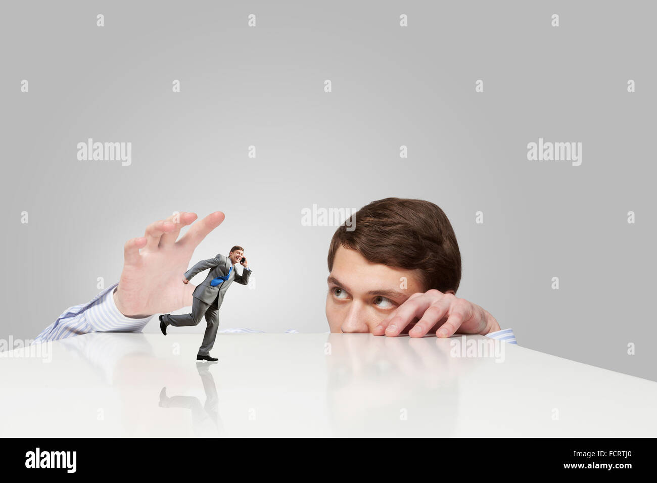 Young man looking from under table and catching running businessman ...