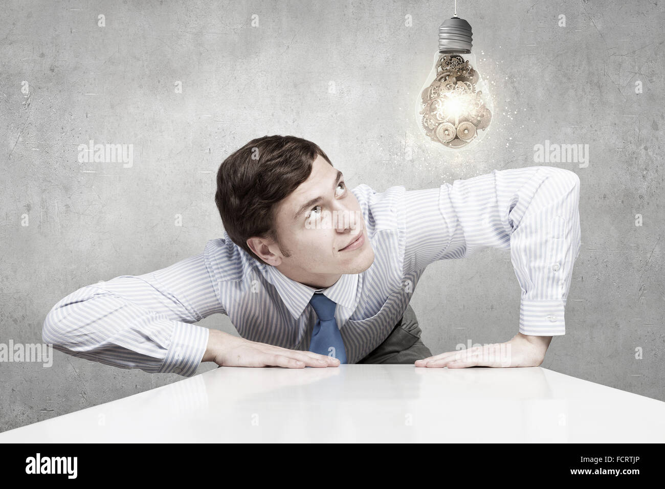 Young man looking from under table on light bulb Stock Photo - Alamy