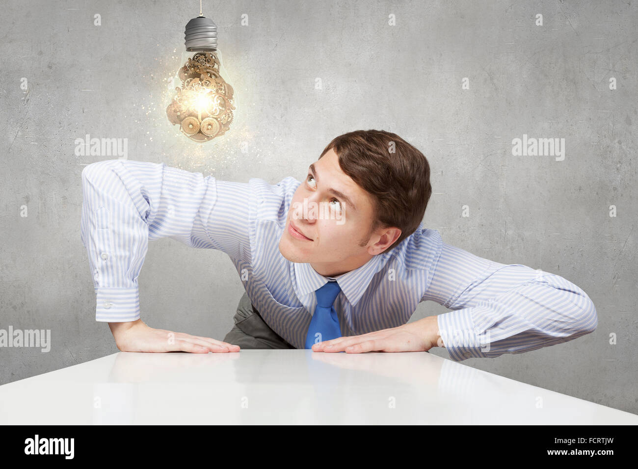 Young man looking from under table on light bulb Stock Photo - Alamy