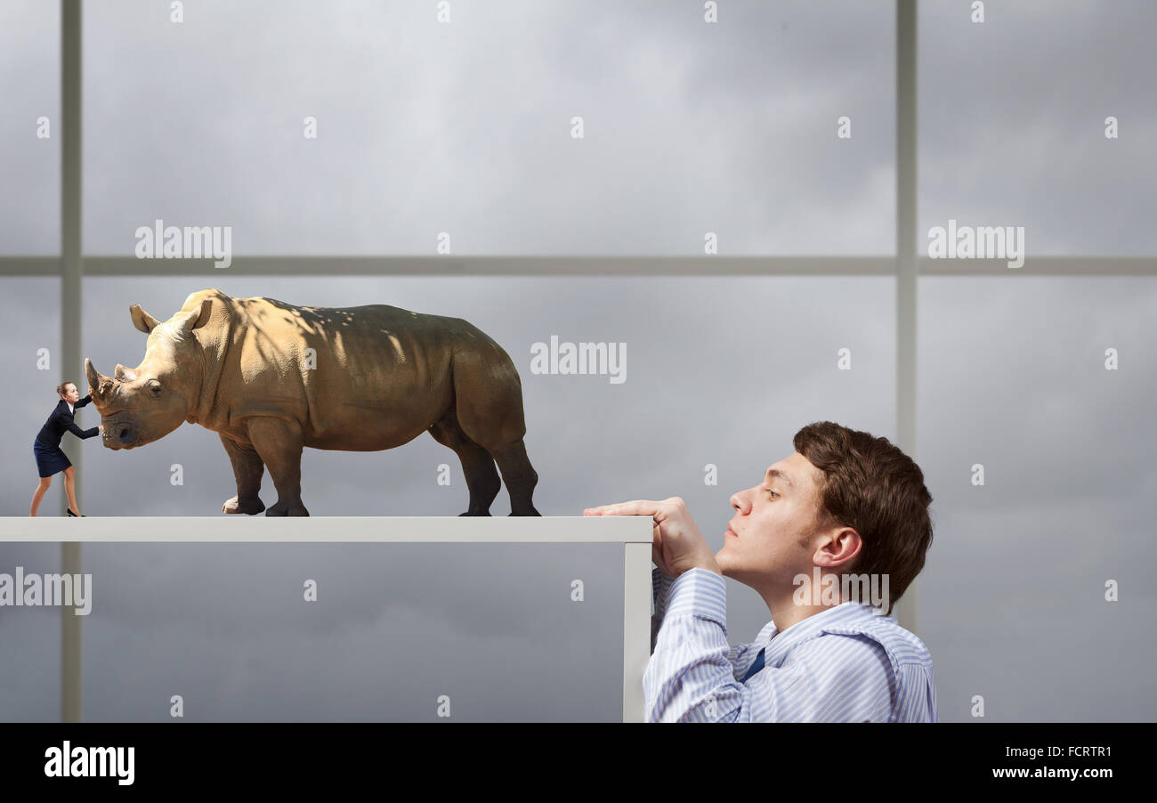 Young man looking from under table on woman fighting with massive rhino ...