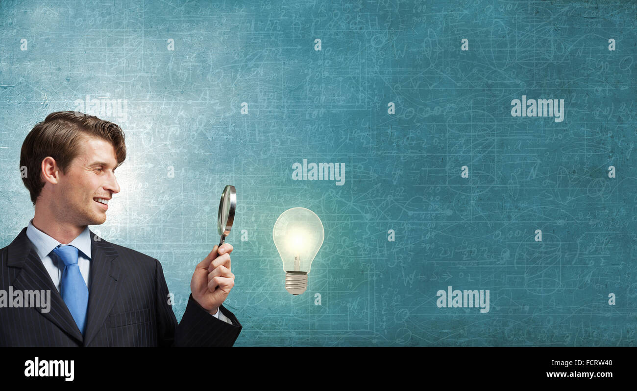 Young smiling man looking in magnifying glass Stock Photo - Alamy