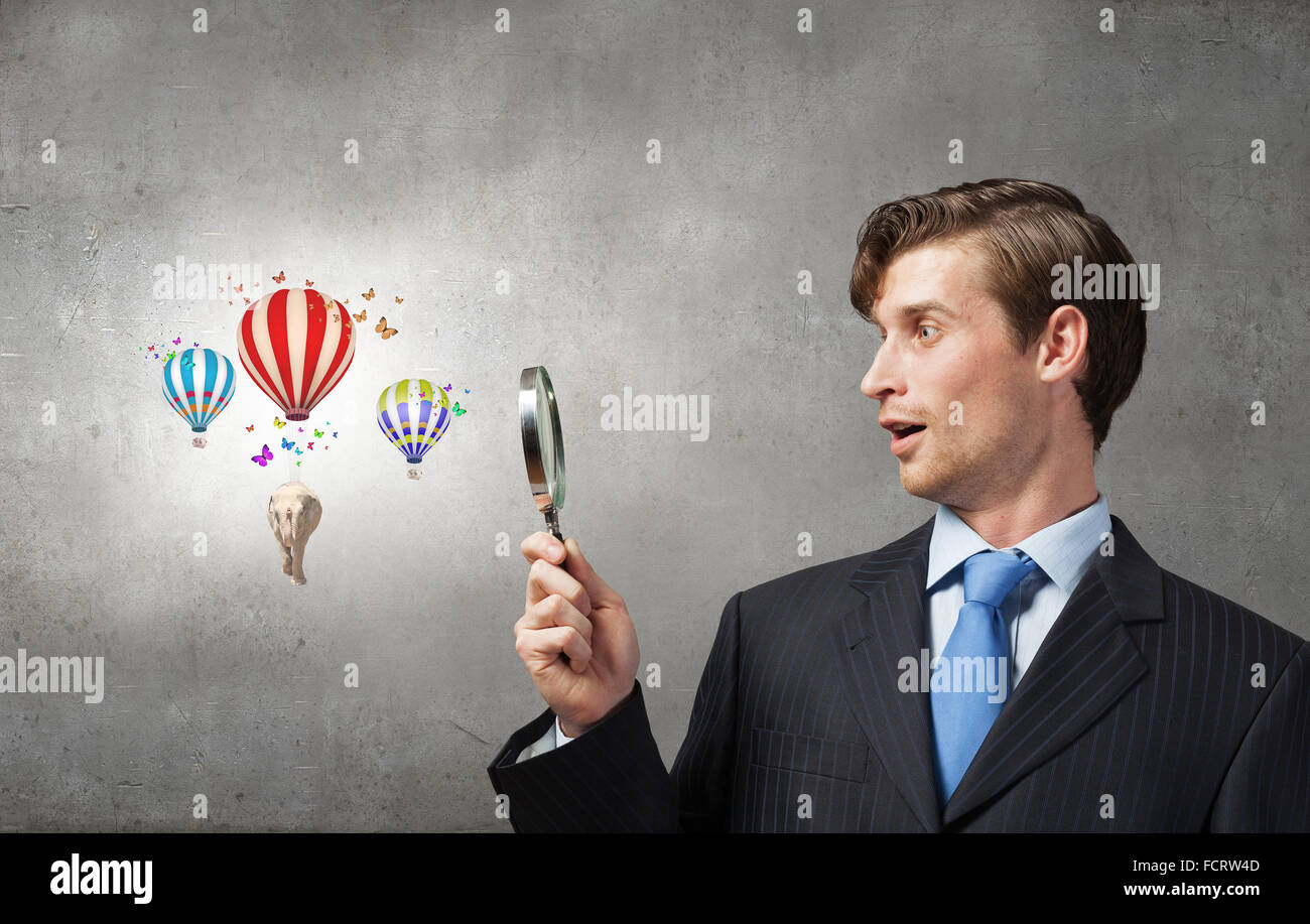 Young smiling man looking in magnifying glass Stock Photo - Alamy