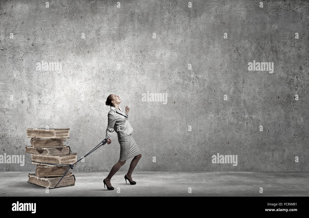 Young businesswoman with ropes on hands pulling pile of books Stock ...