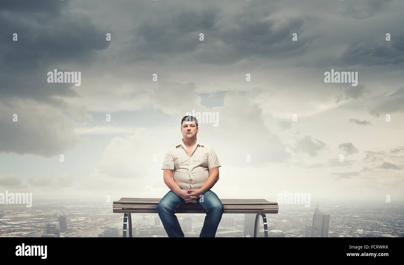 Fat man sitting on bench and looking away Stock Photo - Alamy