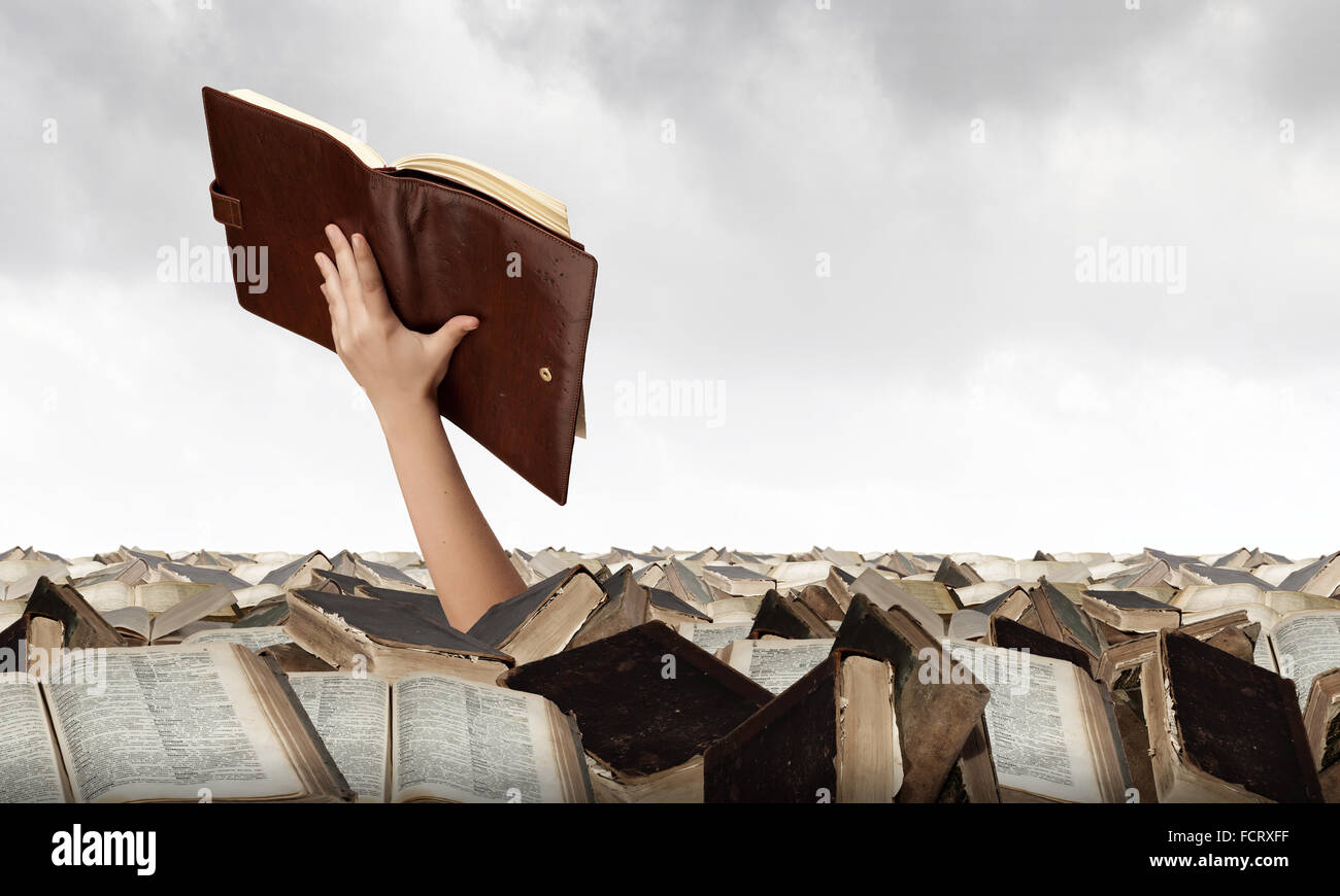 Hand with book reaching out from pile of old books Stock Photo - Alamy