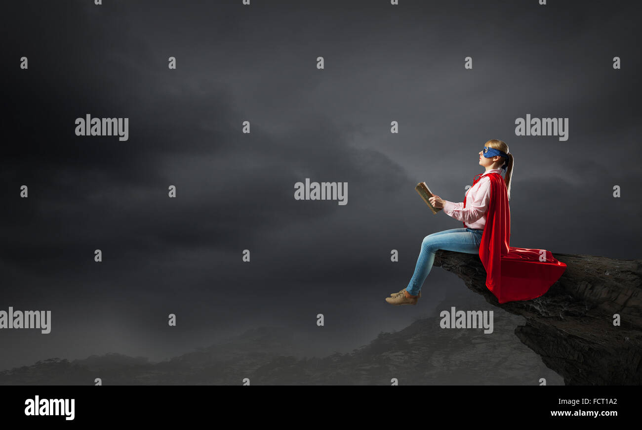 Young woman in super hero costume reading book Stock Photo - Alamy