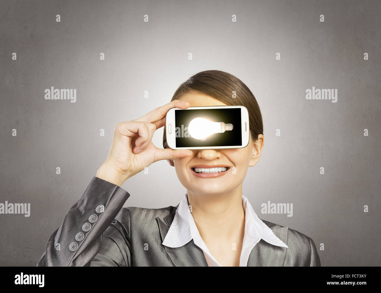 Beautiful young woman holding mobile phone against her eyes and smiling ...