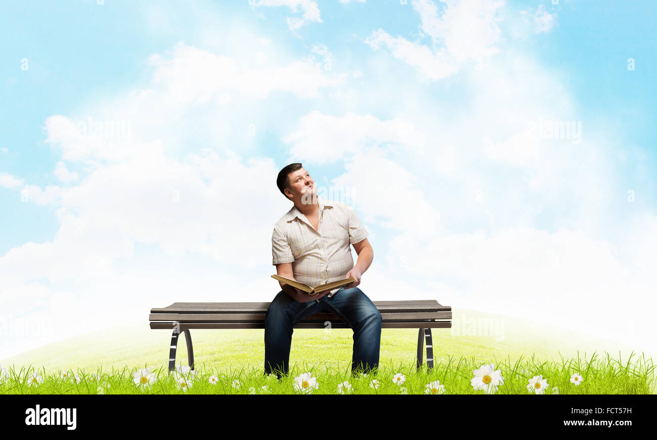 Fat man sitting on bench with book and looking away Stock Photo - Alamy