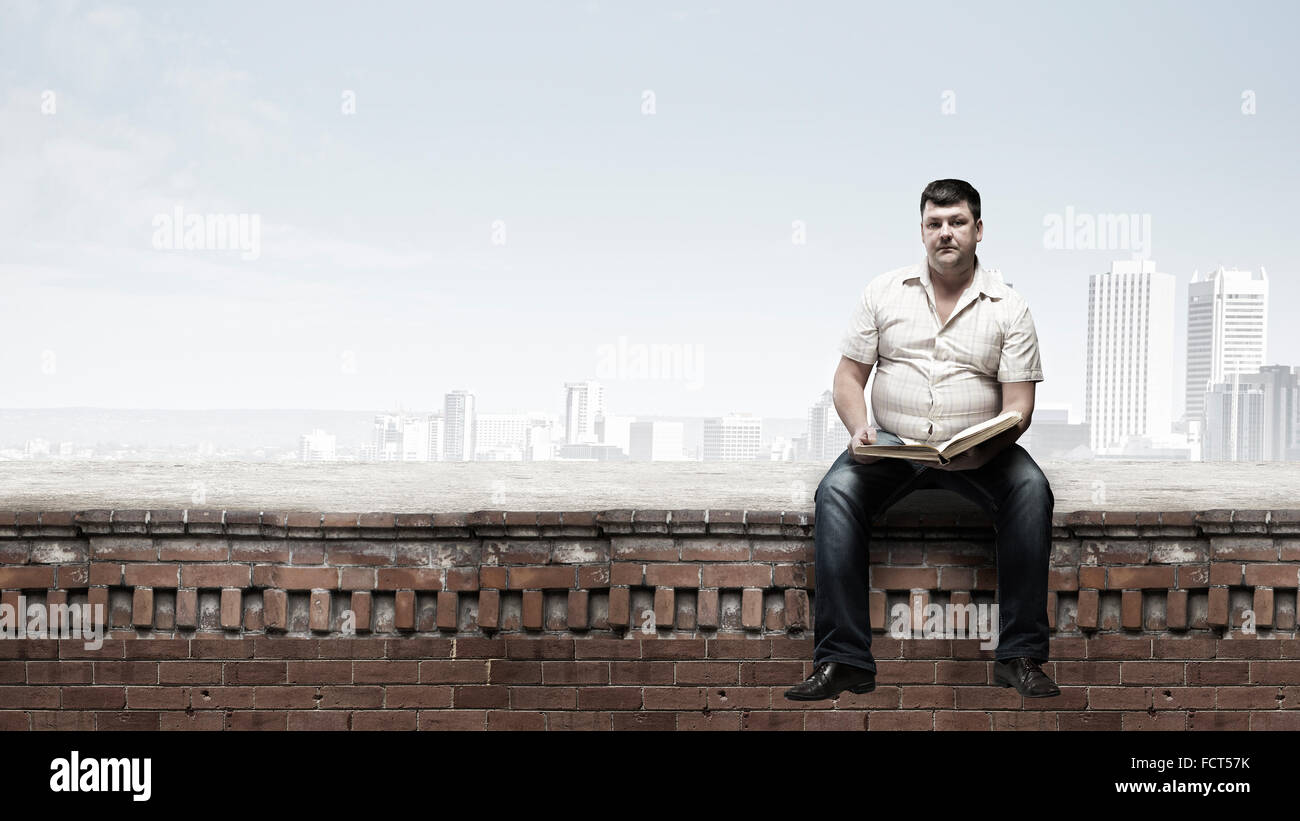 Fat man sitting on building top with book in hands Stock Photo - Alamy