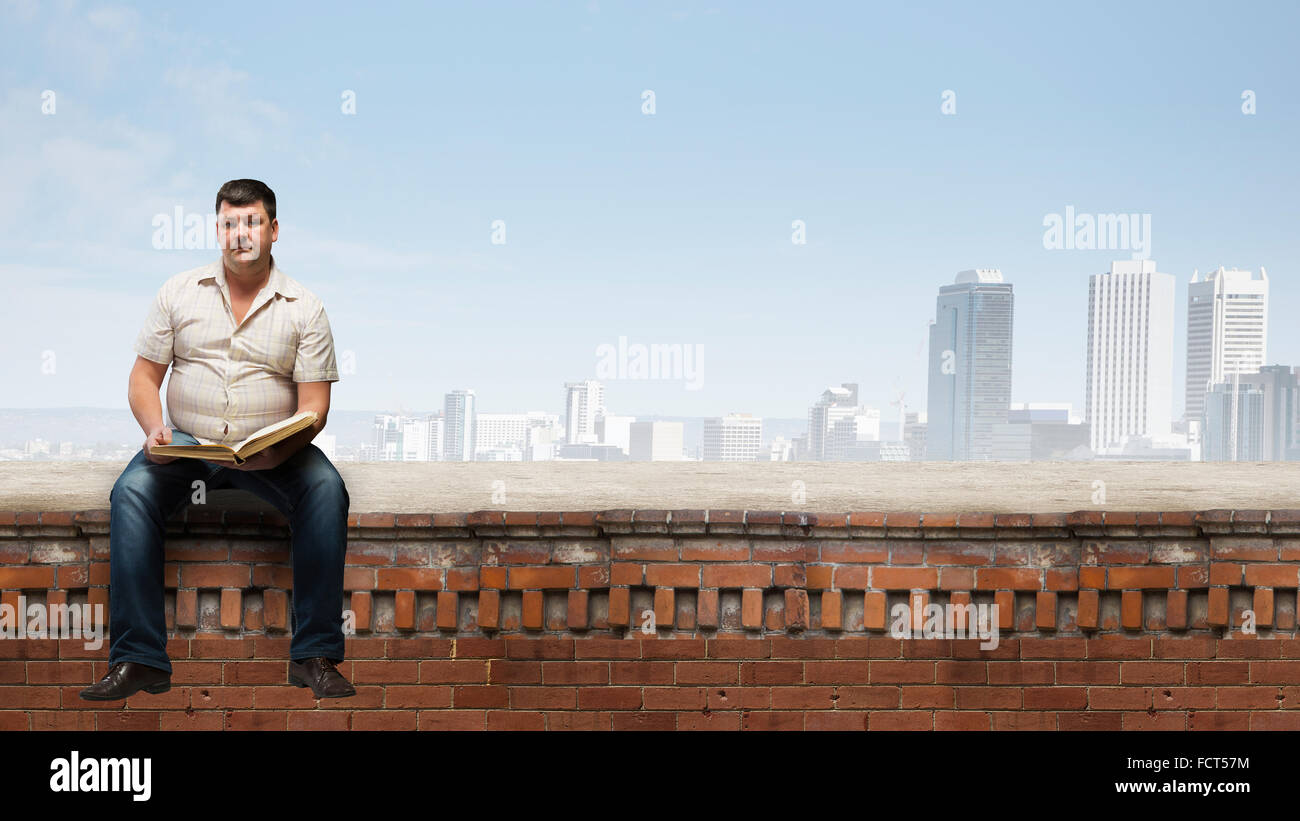 Fat man sitting on building top with book in hands Stock Photo - Alamy