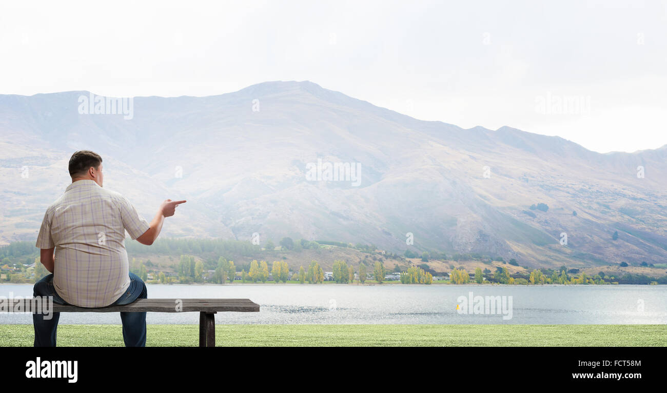 Fat man sitting on bench with his back and pointing away with finger ...