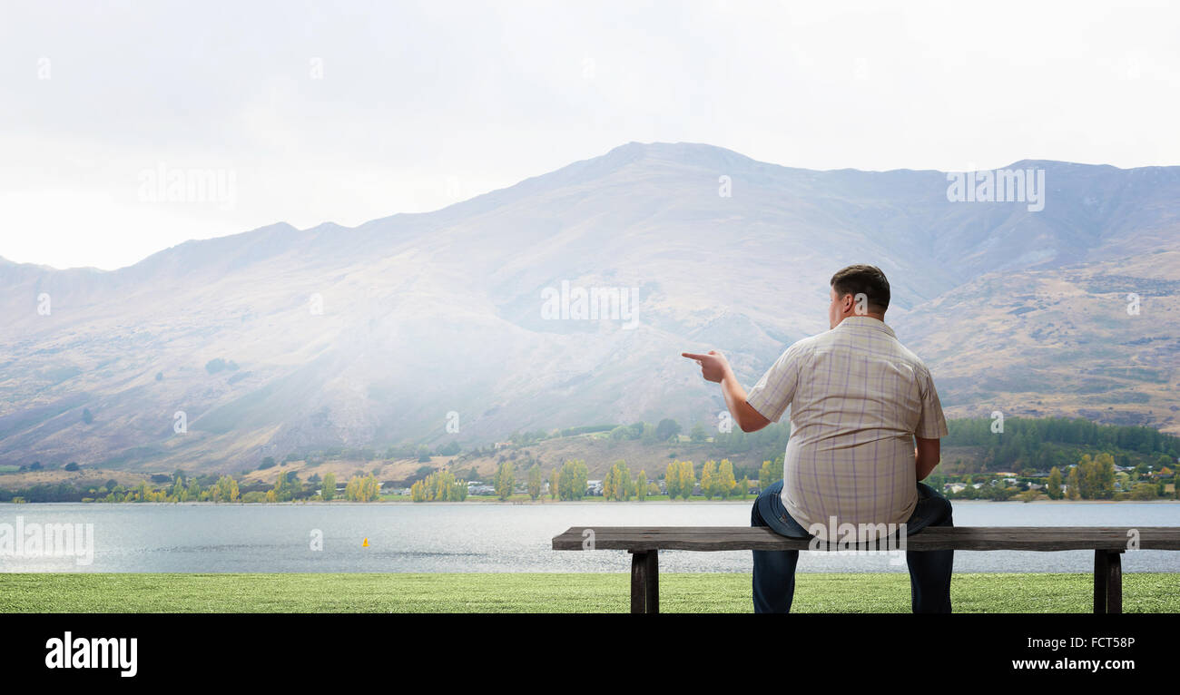 Fat man sitting on bench with his back and pointing away with finger ...