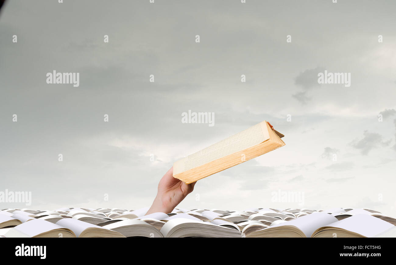 Hand with book reaching out from pile of old books Stock Photo - Alamy
