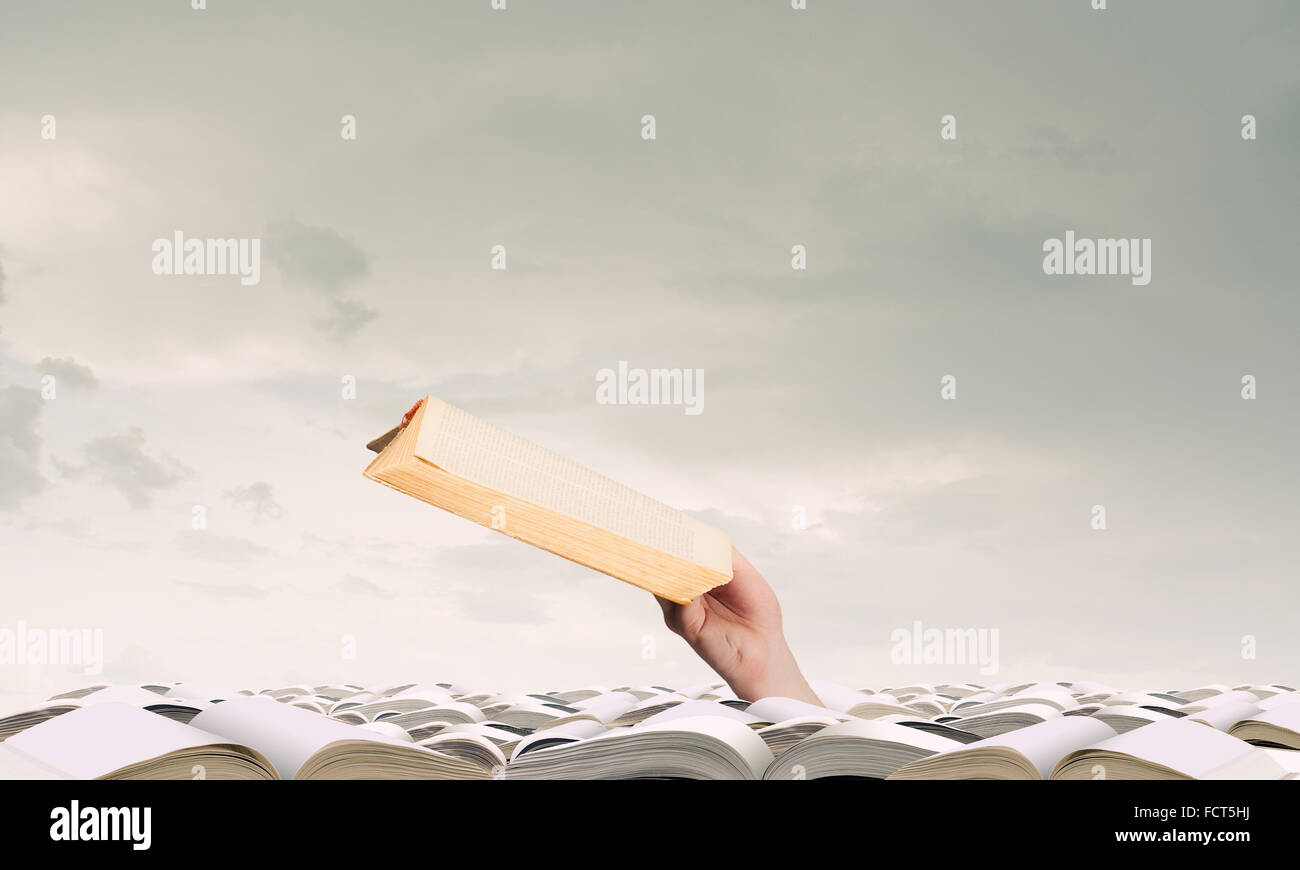 Hand with book reaching out from pile of old books Stock Photo - Alamy