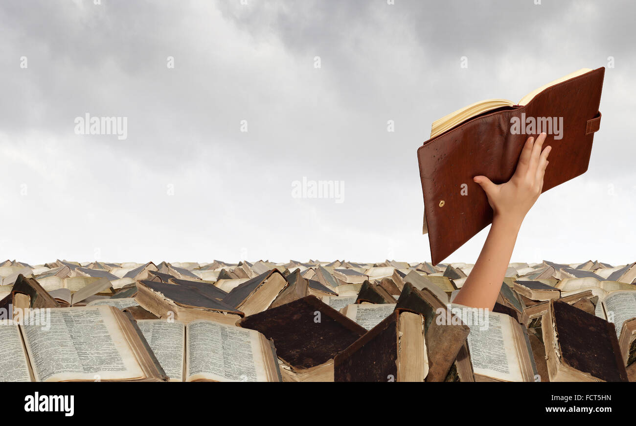 Hand with book reaching out from pile of old books Stock Photo - Alamy