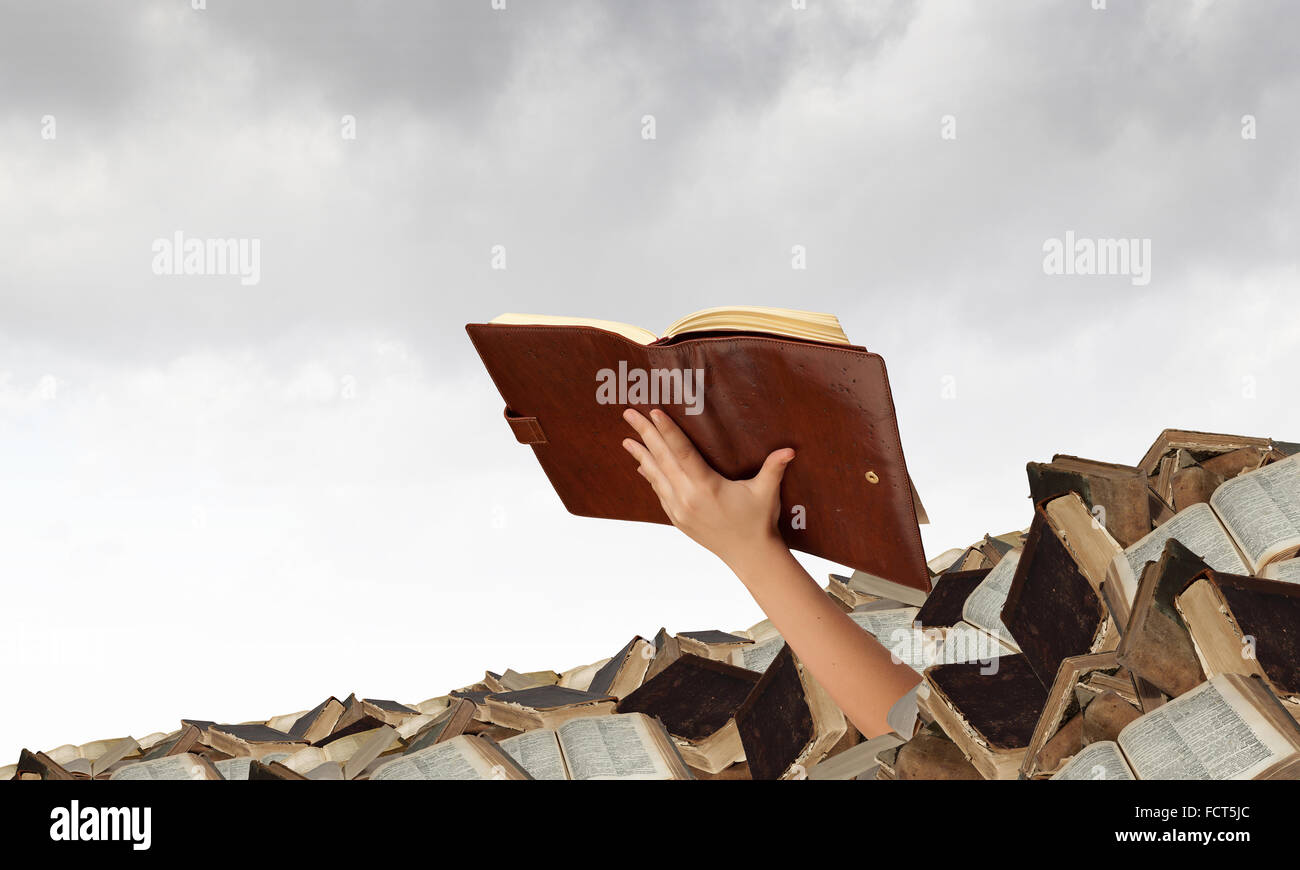 Hand with book reaching out from pile of old books Stock Photo - Alamy