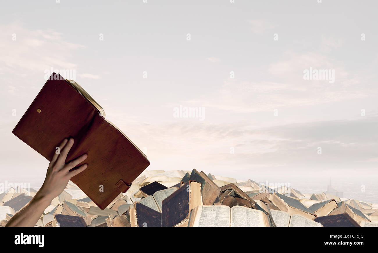 Hand with book reaching out from pile of old books Stock Photo - Alamy