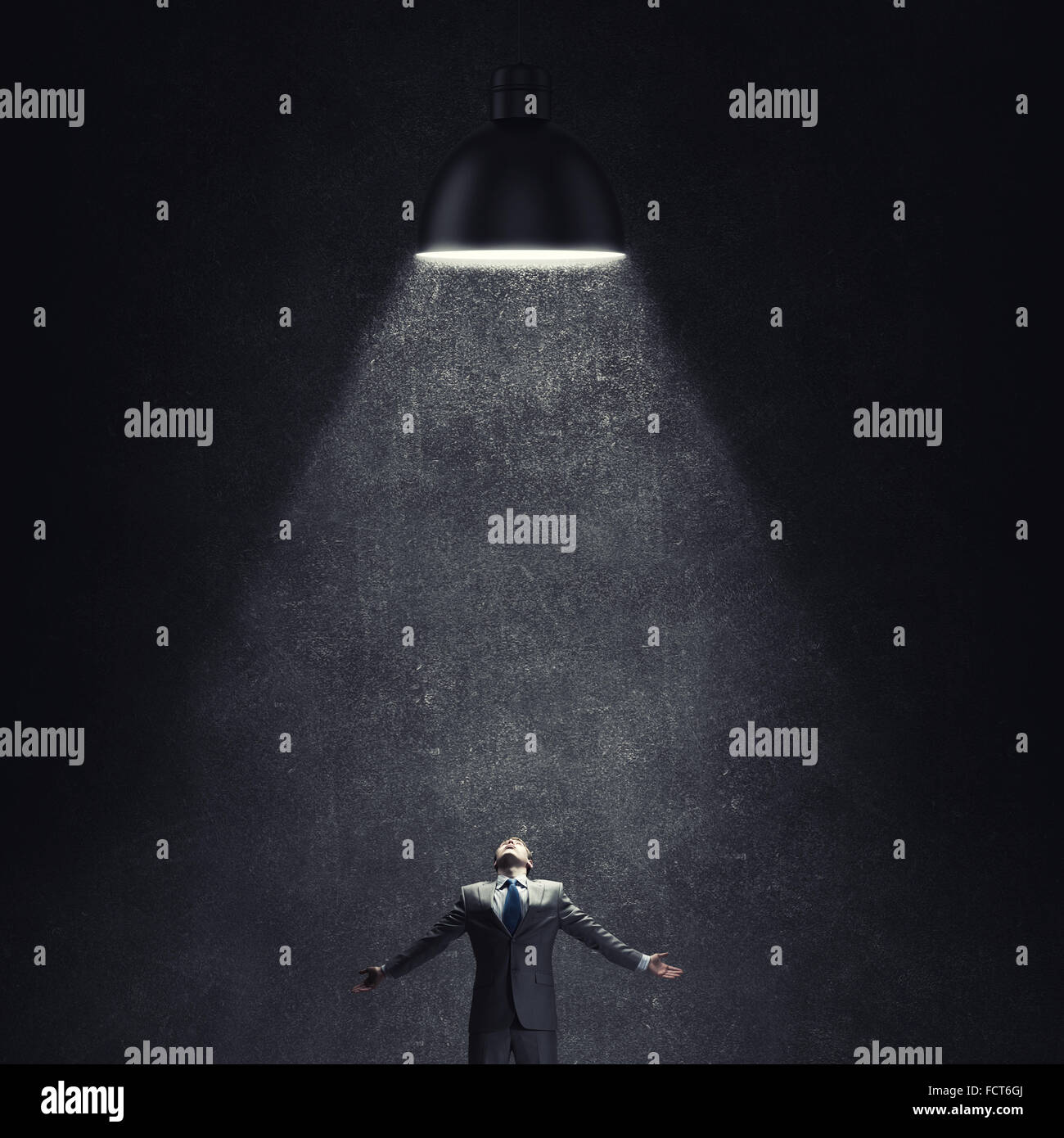 Businessman with hands spread apart standing in light coming from above ...