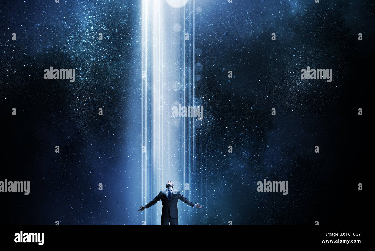 Businessman with hands spread apart standing in light coming from above ...