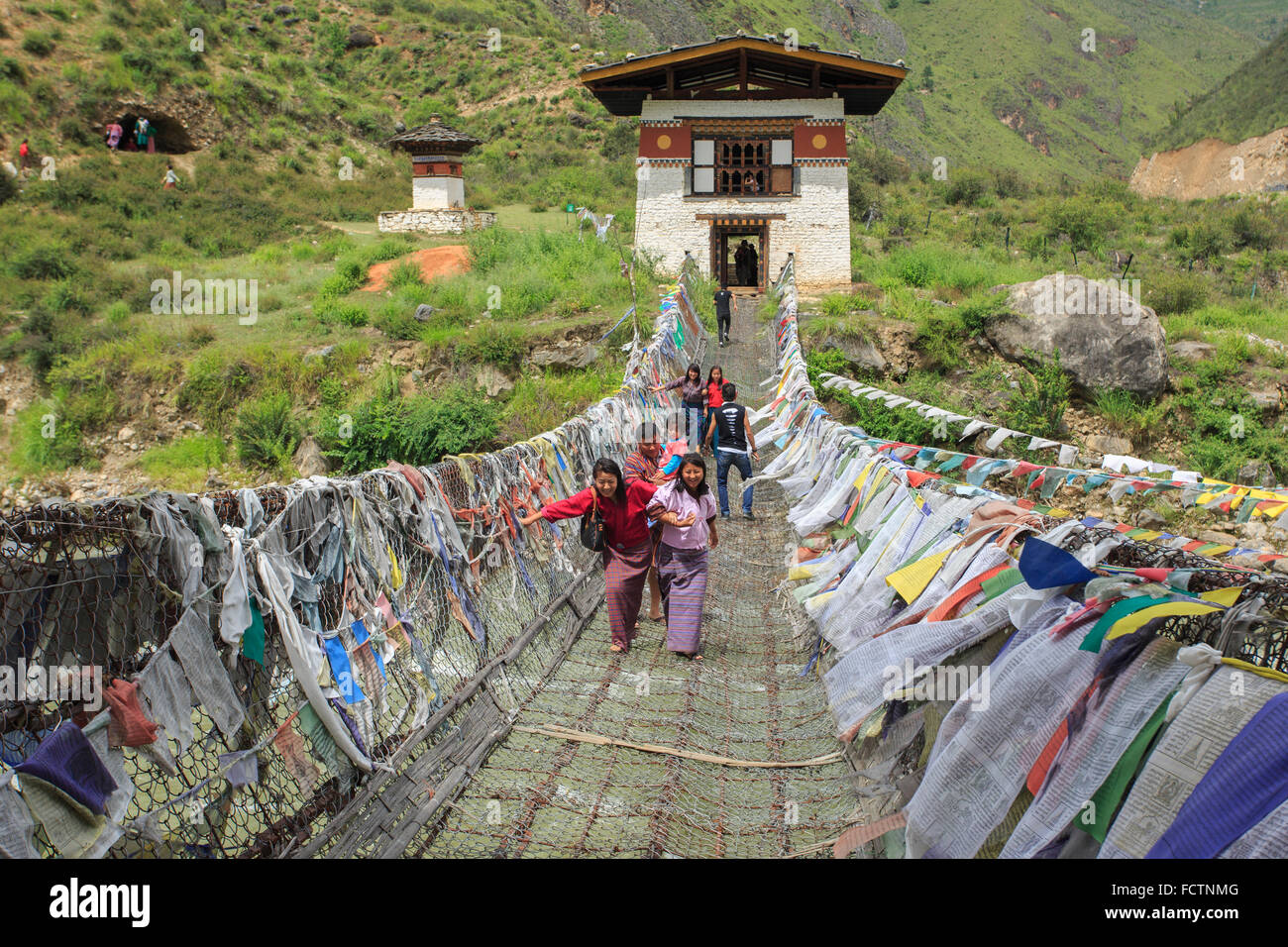 People crossing a wire suspension bridge crosses a river in Bhutan, on ...