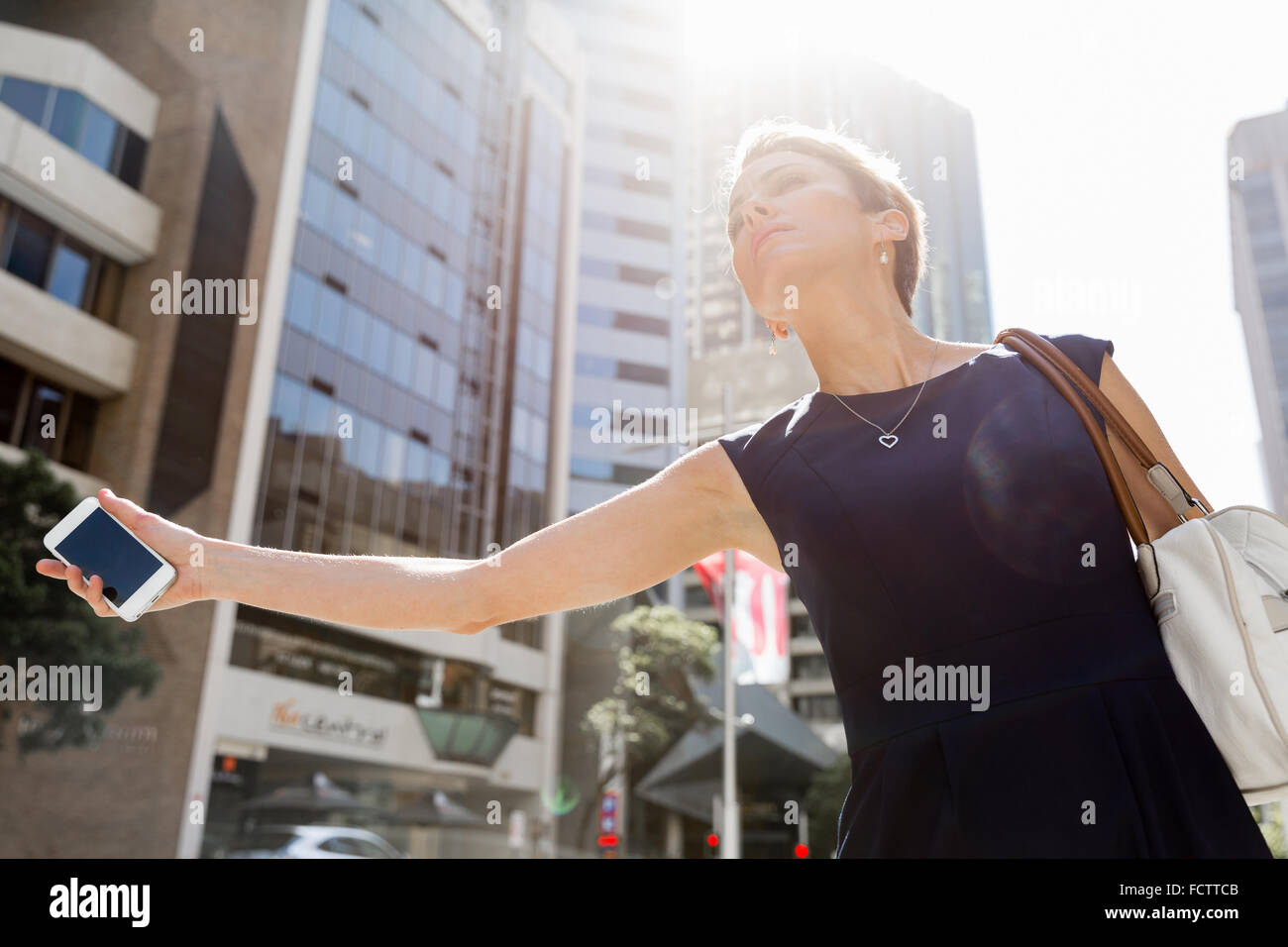 Businesswoman in a city street waving for taxi Stock Photo - Alamy