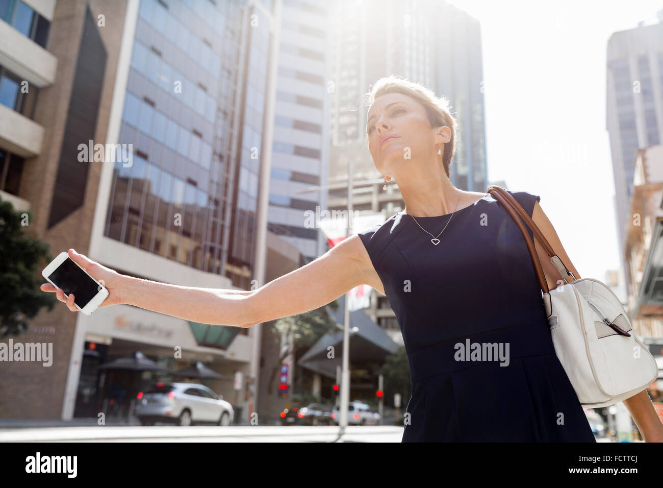 Businesswoman in a city street waving for taxi Stock Photo - Alamy