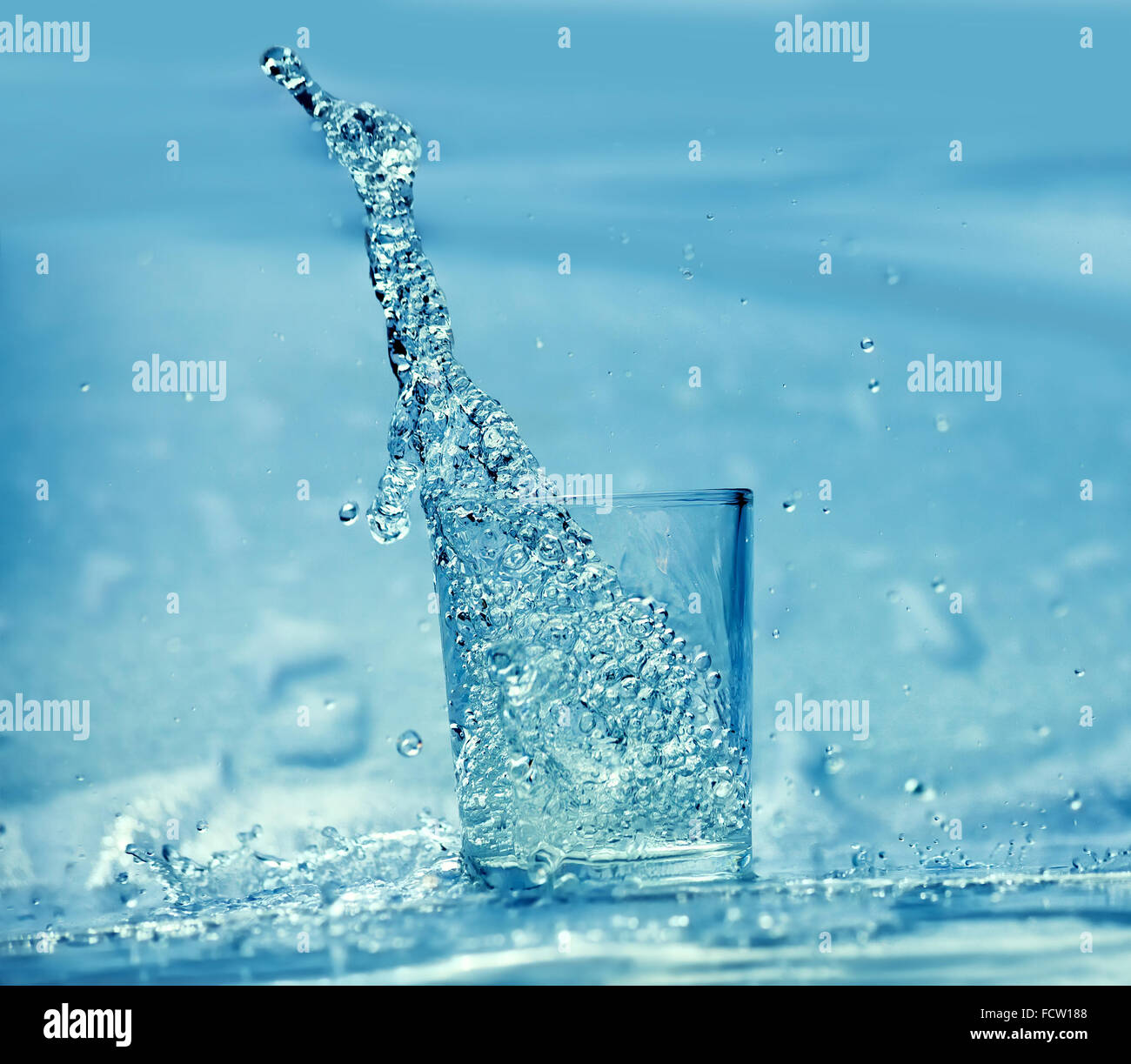 Splashing water from glass on blue background Stock Photo - Alamy