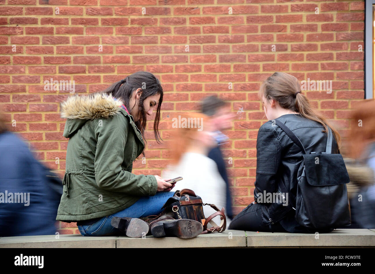 Two teenage girls sat on a wall together while the rest of the world ...