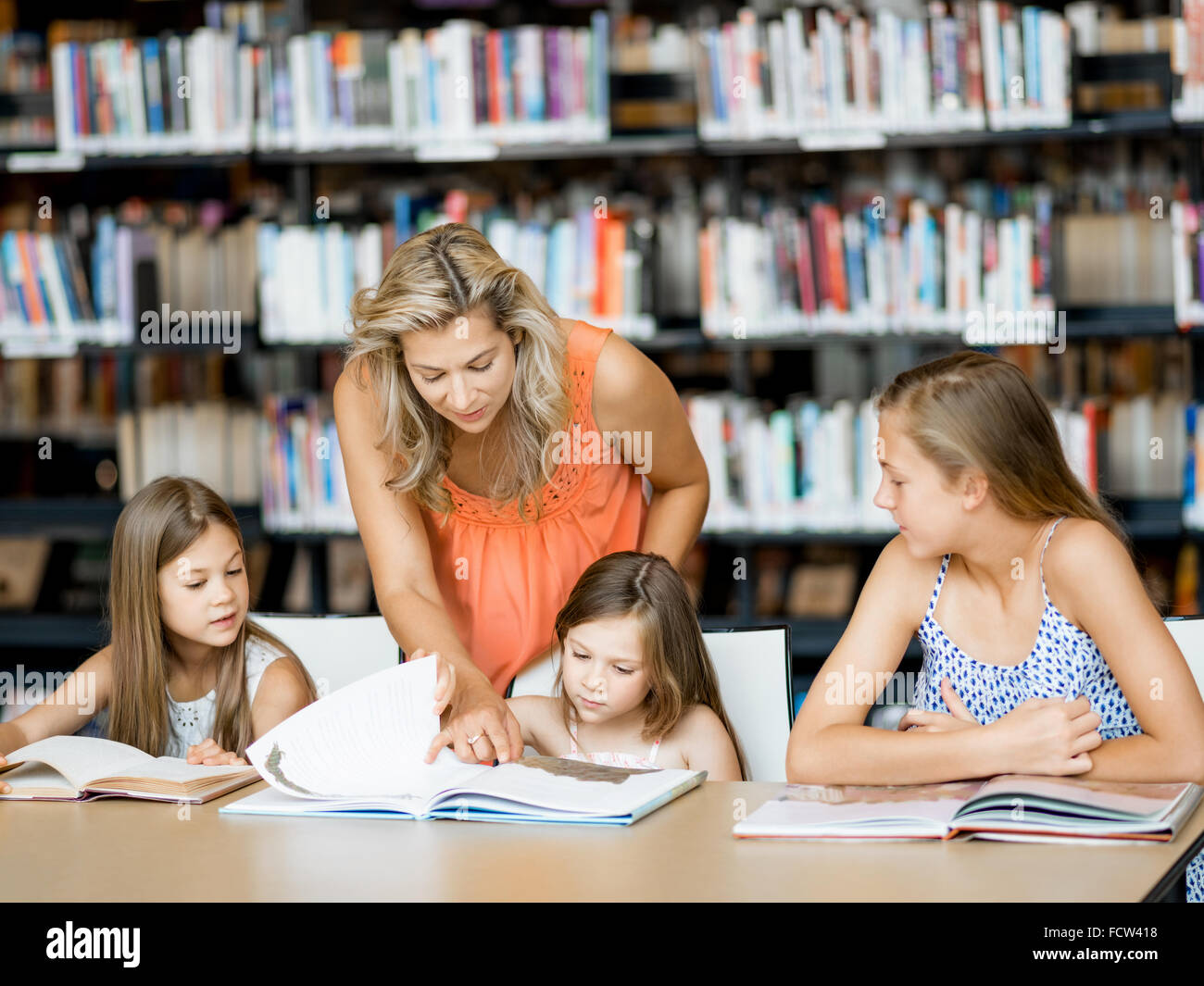 Little girls with their mother reading books in library Stock Photo - Alamy
