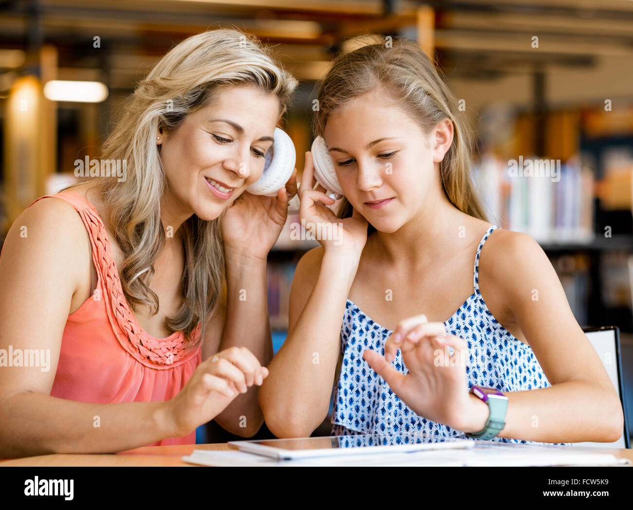 A teenage girl with headphones sitting in a library with her mum Stock ...