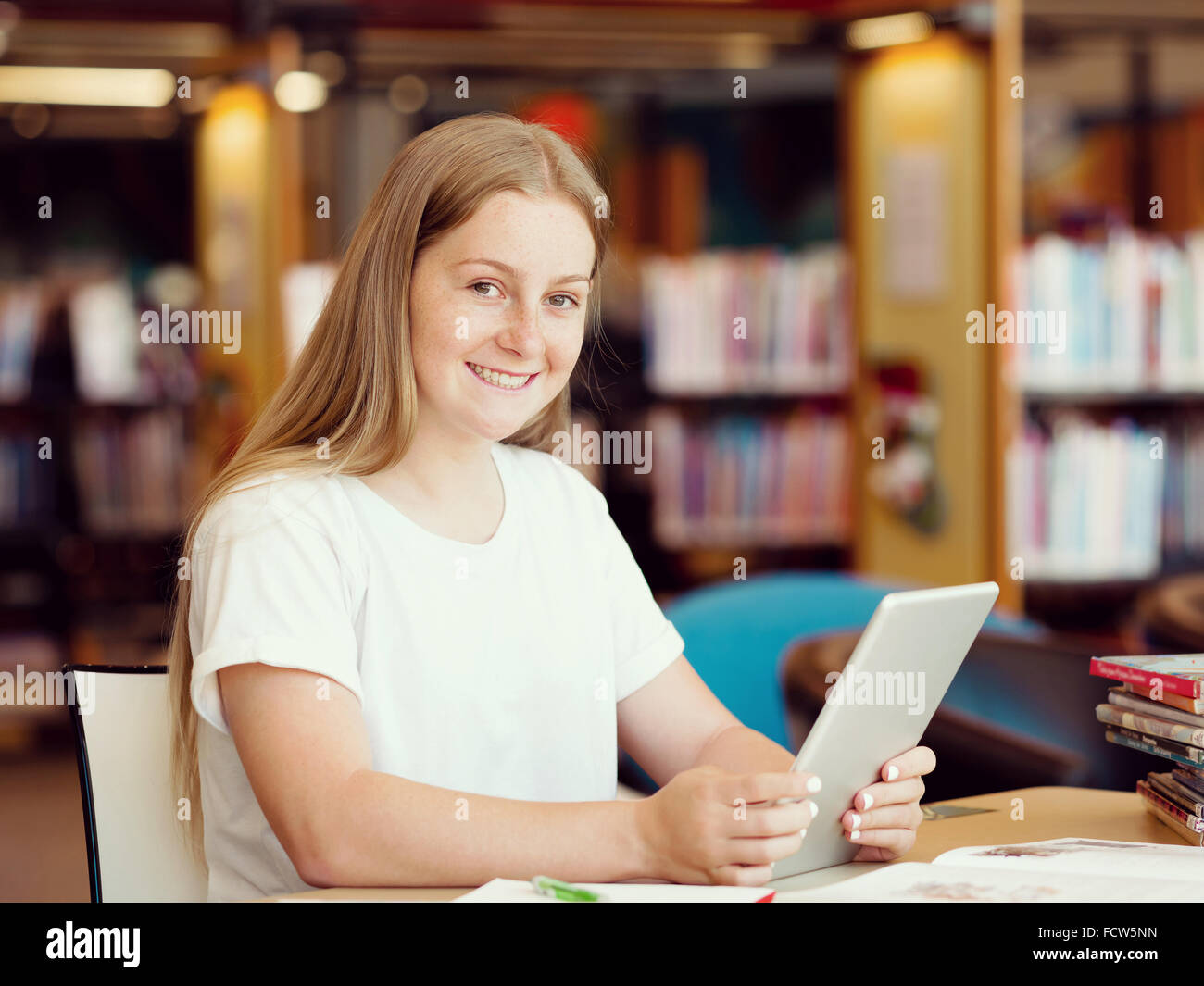 Teenage girl sitting with tablet in library Stock Photo - Alamy
