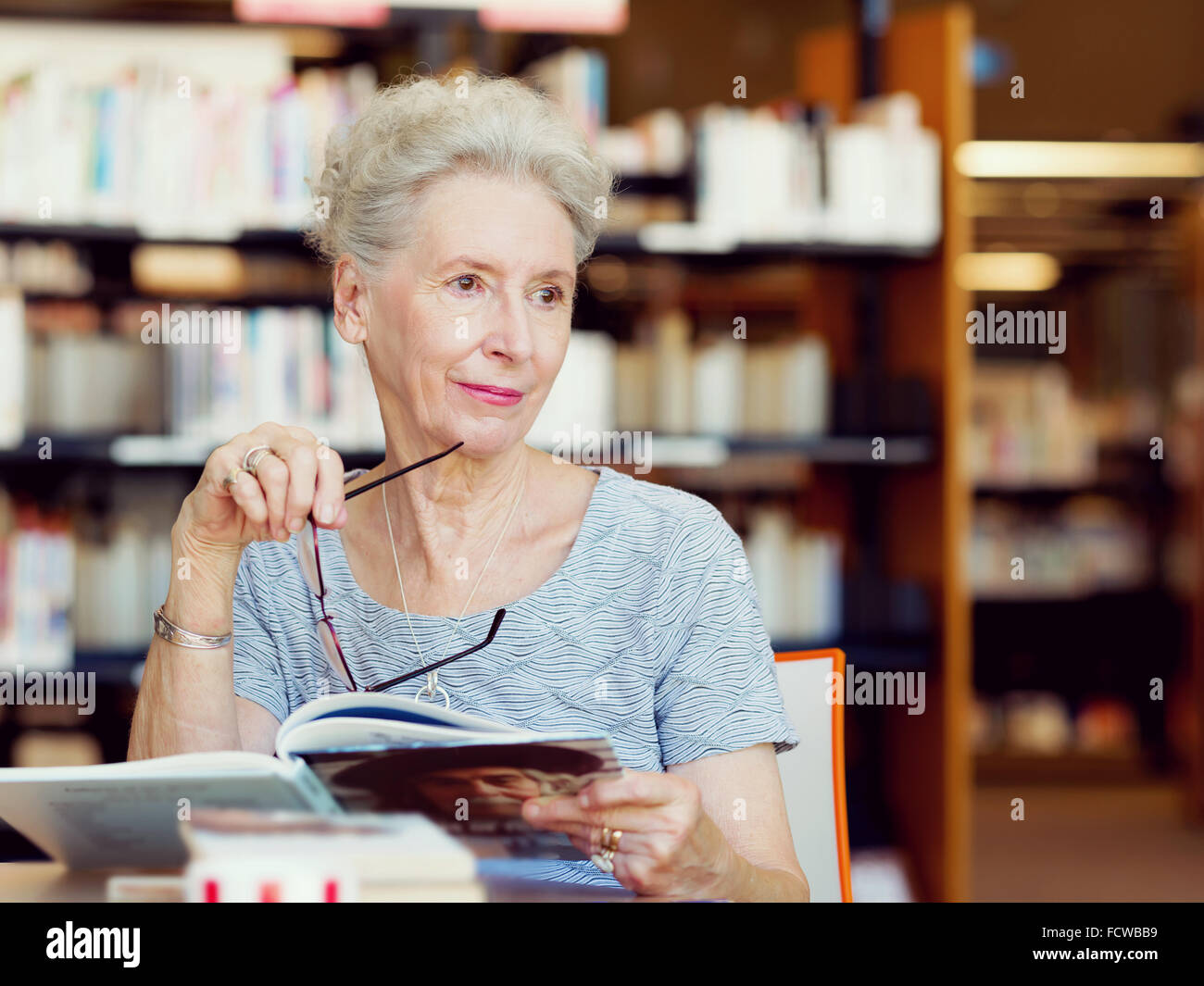 Elderly lady reading books in library Stock Photo - Alamy