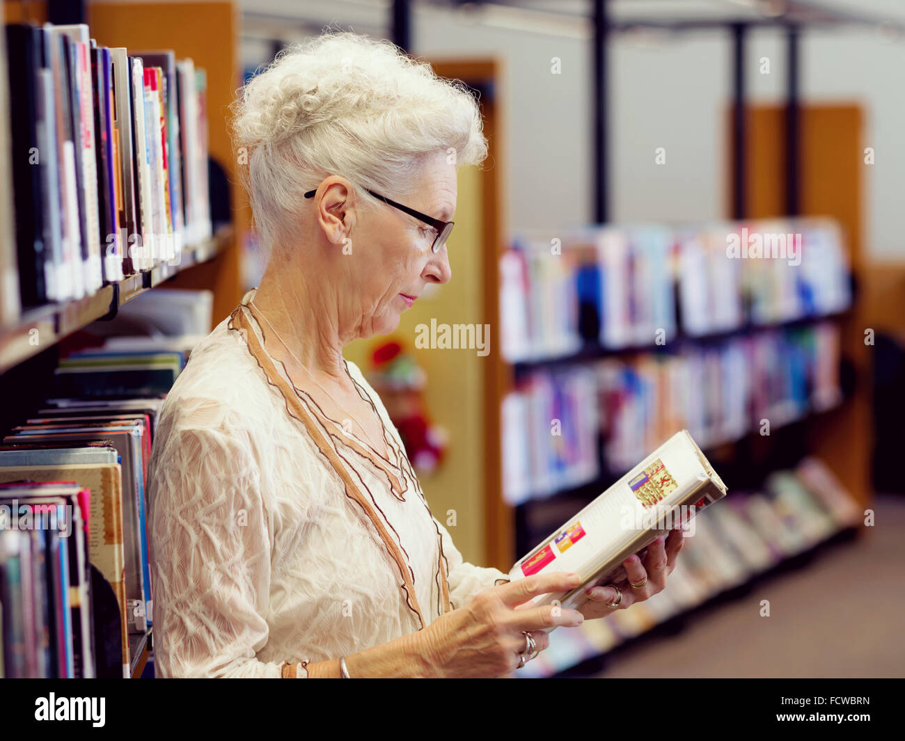 Elderly lady standing next to book shelves in library Stock Photo - Alamy