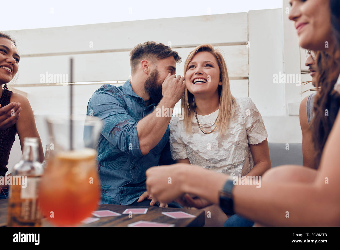 Young people sitting together in a party. Man whispering something in ...