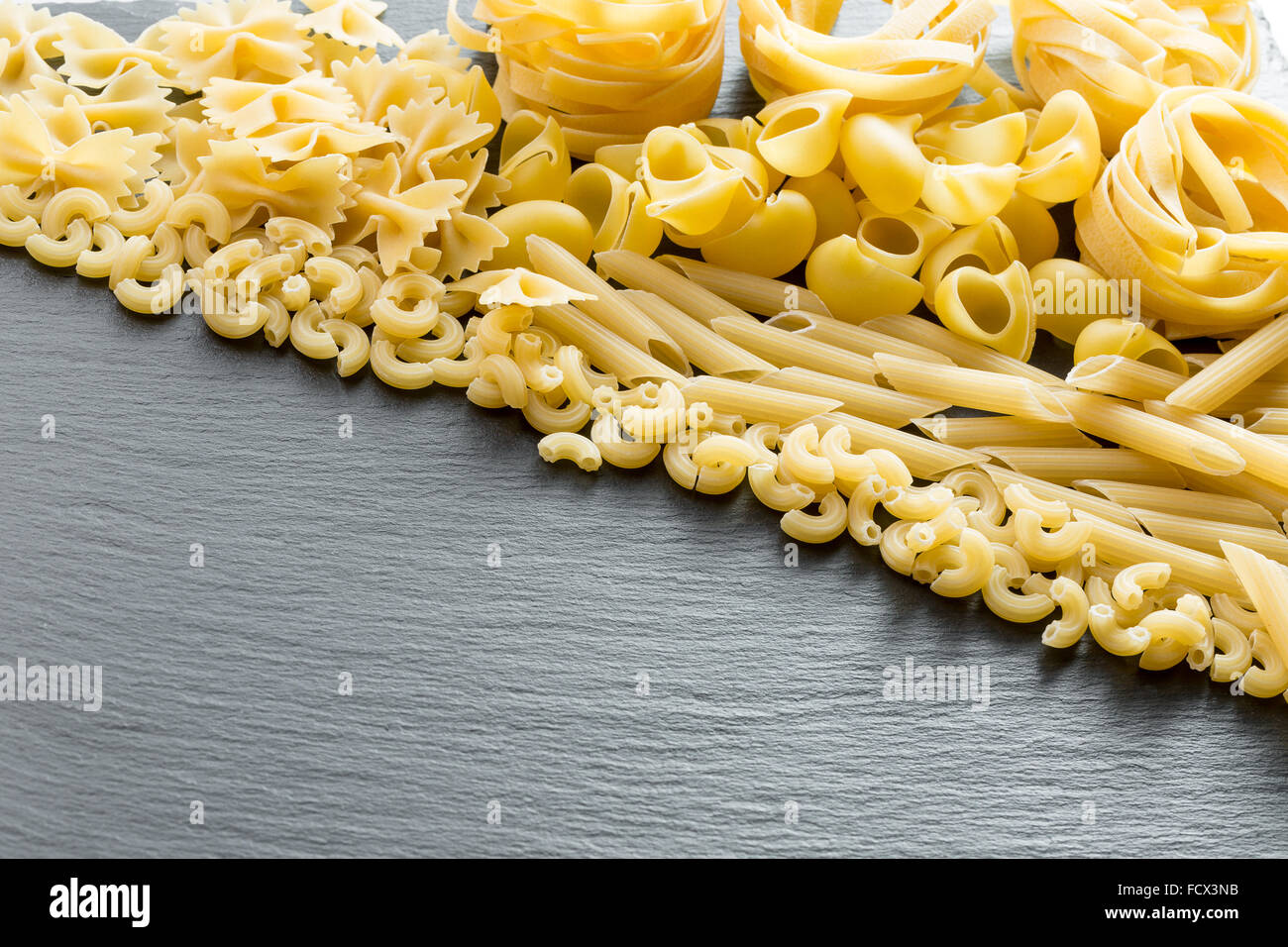 Variety of types and shapes of Italian pasta on a dark stone background ...