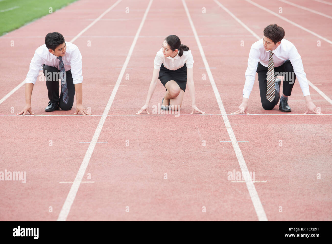 Two men and a woman in business wear being about to run on a track with ...
