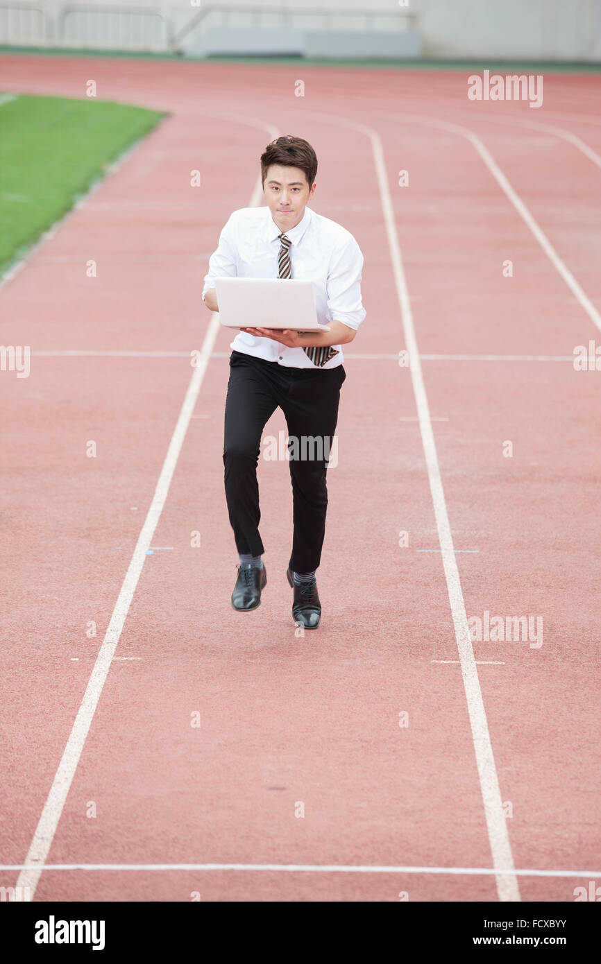 Man in business wear running on a track while working on a laptop Stock ...