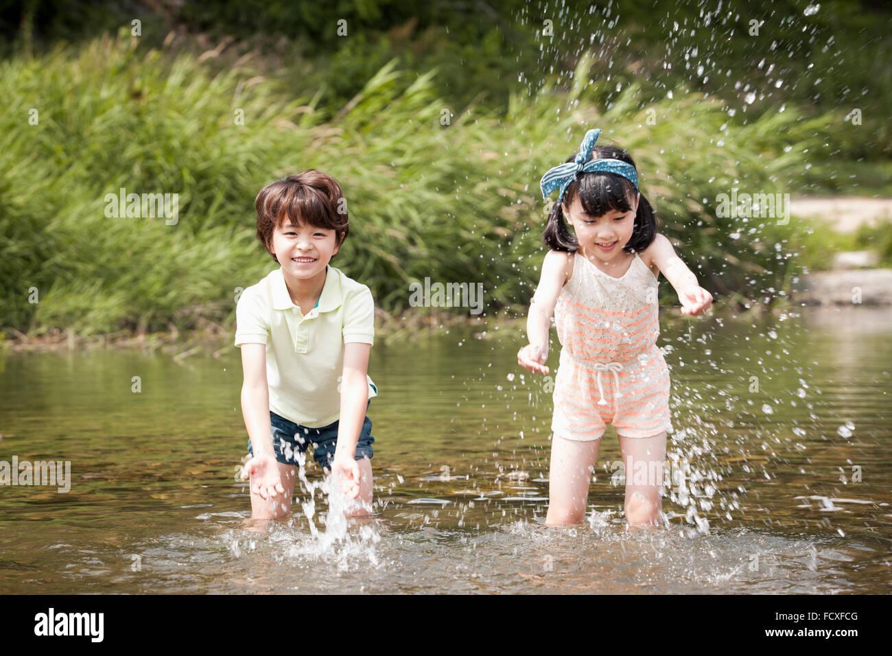 Boy and a girl playing in the water of the stream enjoying their summer ...